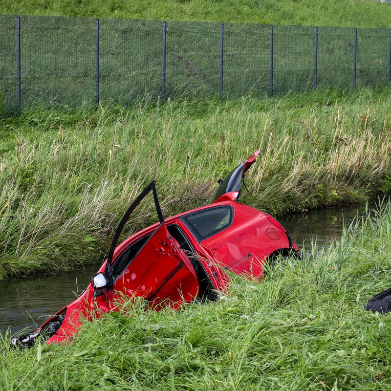 Auto rijdt in sloot, meerdere voorbijgangers springen in het water en ...